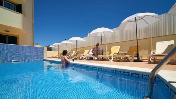 Piscina com chão azul ladrilhado, espreguiçadeiras e guarda-sóis.