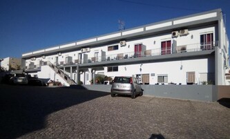 Um edifício de vários andares com uma escadaria central, um carro estacionado em frente e um céu azul e límpido.