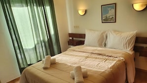 Uma cama bem arrumada com duas toalhas enroladas, uma mesa de cabeceira com abajur e um quadro na parede.