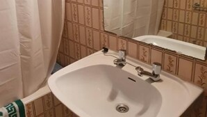 Casa de banho com lavatório branco, espelho e azulejos estampados.
