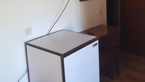 Um quarto pequeno com televisão na parede, uma escrivaninha e uma cadeira.
