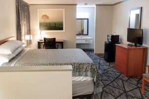 Quarto de hotel com uma cama, escrivaninha, cômoda, televisão e espelho.