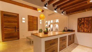 Uma cozinha moderna com ilha de madeira, luminárias pendentes e um quadro grande na parede.