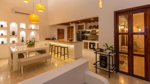 Uma cozinha moderna com ilha central, banquetas, luminárias pendentes e uma área de refeições com bancos.