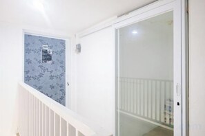 Um quarto com porta branca, janela estampada com flores e corrimão branco.