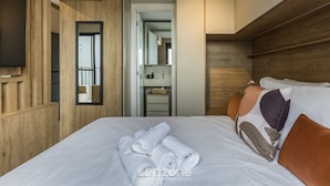 Quarto de hotel com cabeceira de madeira, cama bem arrumada com toalhas dobradas, um espelho grande e vista para o banheiro.