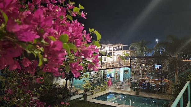 Uma área à beira da piscina, com um espaço de estar coberto, um bar e uma escadaria que dá acesso a um andar superior.