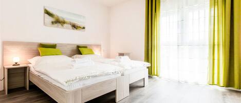 Uma cama de casal com duas almofadas, uma mesa de cabeceira com abajur e uma janela com cortinas.
