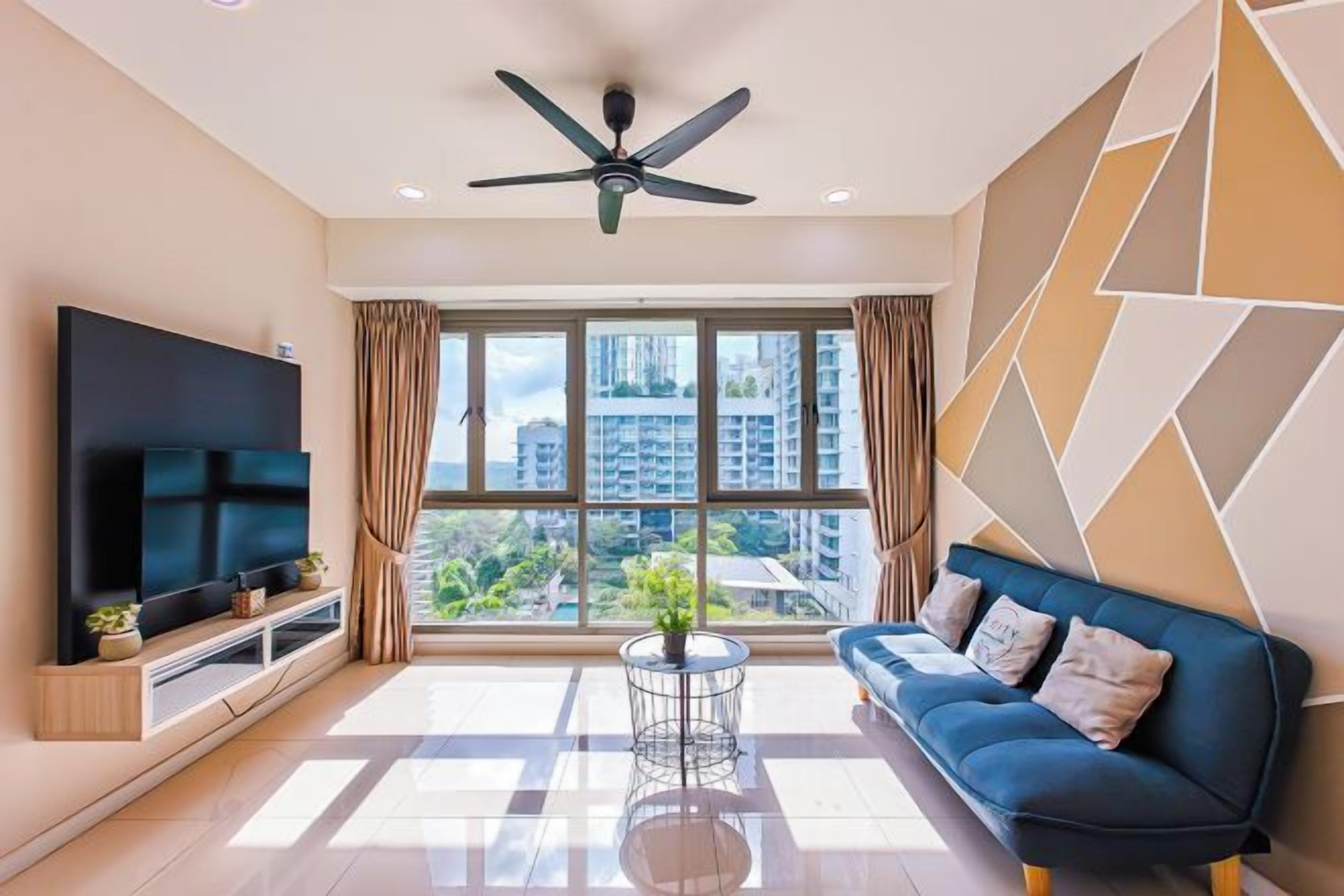 Uma sala de estar moderna com televisão de tela plana, um sofá azul, um ventilador de teto e uma grande janela com cortinas.