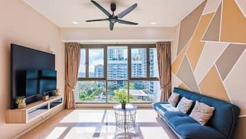 Uma sala de estar moderna com televisão de tela plana, um sofá azul, um ventilador de teto e uma grande janela com cortinas.