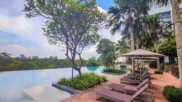 Um deck de madeira com espreguiçadeiras e um toldo, com vista para uma piscina cristalina e palmeiras ao fundo.