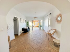 Uma sala ampla com um sofá preto, uma poltrona de vime e uma mesa de jantar.