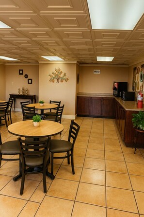 Uma área de refeições com mesas e cadeiras redondas, um espaço de cozinha e uma parede com o letreiro 'Mito'.