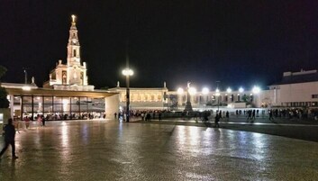 Uma praça com um grande edifício, destacando-se uma torre e uma estátua.
