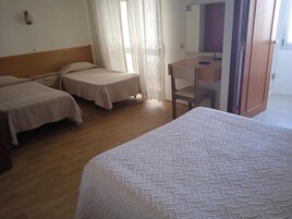 Quarto de hotel com duas camas de solteiro, cabeceira de madeira, uma pequena escrivaninha com cadeira e uma porta de vidro corria para uma varanda.