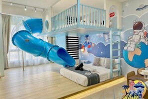 Uma área de recreação infantil com escorrega, beliches e um mural de um astronauta.