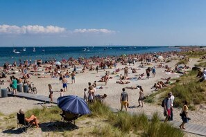 Uma praia lotada com pessoas tomando sol e passeando.