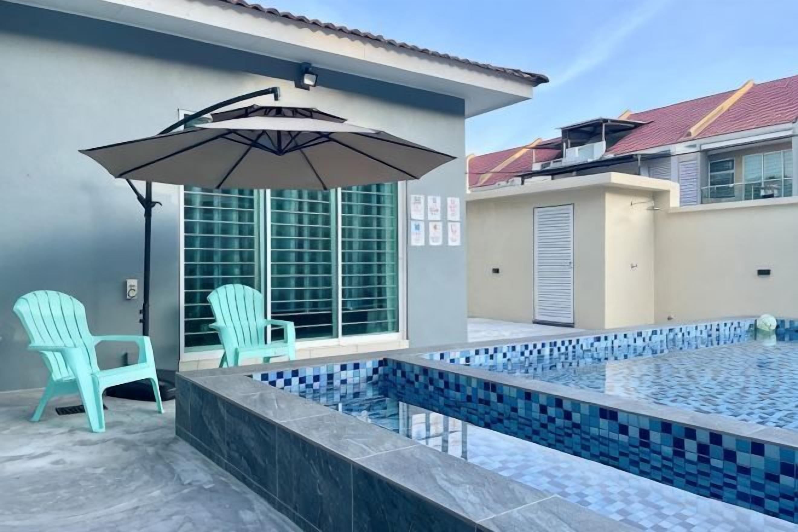 Piscina com bordas azulejadas, duas cadeiras e um guarda-sol de patamar.