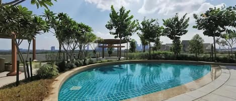 Piscina com borda azulejada, rodeada por vegetação e uma estrutura de pérgola.