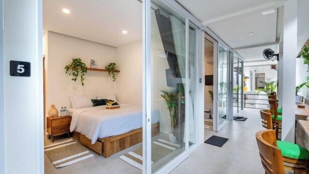 Quarto moderno com cama, mesa de cabeceira e porta de vidro deslizante que dá para uma sala de jantar.