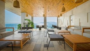 Um interior moderno com teto de madeira, mesas, cadeiras e vista para o mar.