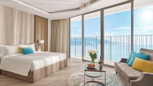 Quarto de hotel com cama grande, sofá, mesa de centro e vista para o mar.