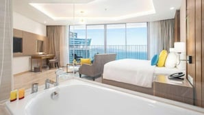Quarto de hotel moderno com uma cama grande, área de estar separada, banheira e vista para a cidade.
