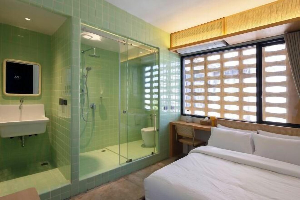 Quarto de hotel com chuveiro envidraçado, pia, vaso sanitário, cama e janela com vista.