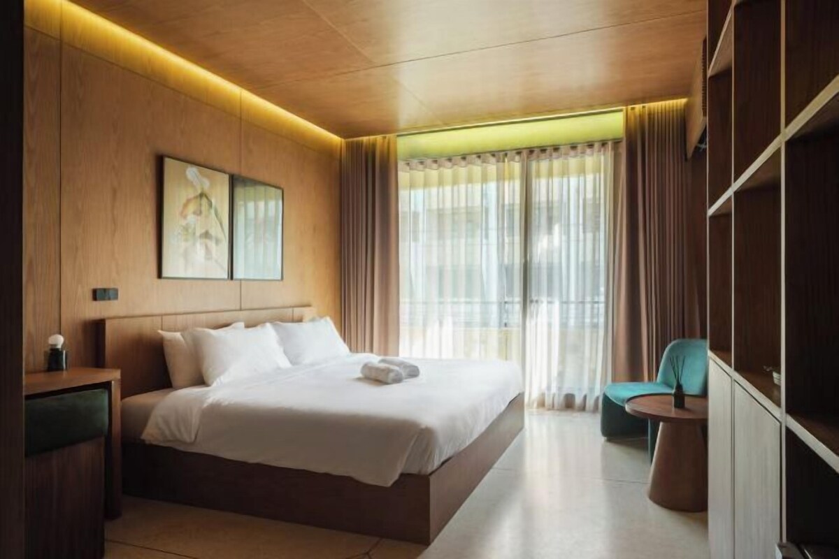 Quarto de hotel com uma cama grande, uma escrivaninha, uma cadeira e uma janela com cortinas.
