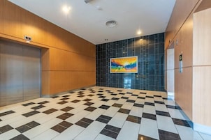 Um corredor com piso xadrez, um quadro na parede e uma porta à esquerda.