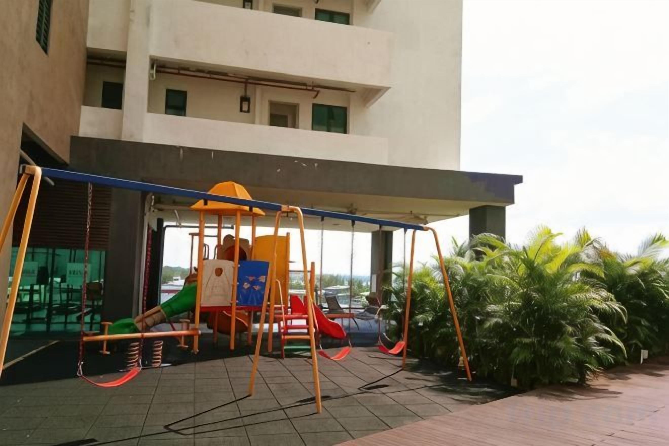 Área de lazer ao ar livre com balanços e escorregadores, em frente a um edifício com entrada coberta.