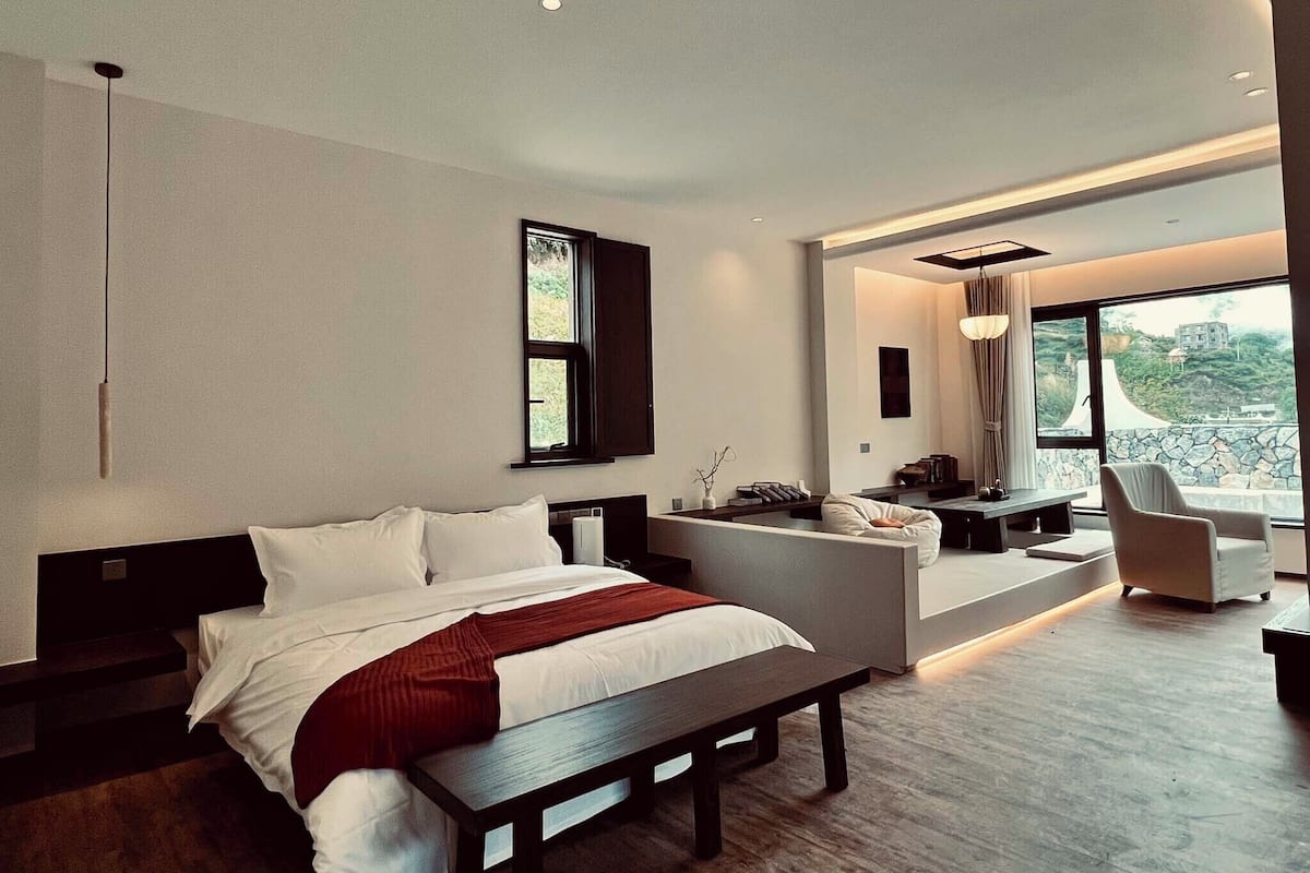 Um quarto moderno com uma cama grande, mesas de cabeceira, um banquinho, uma escrivaninha e uma cadeira.