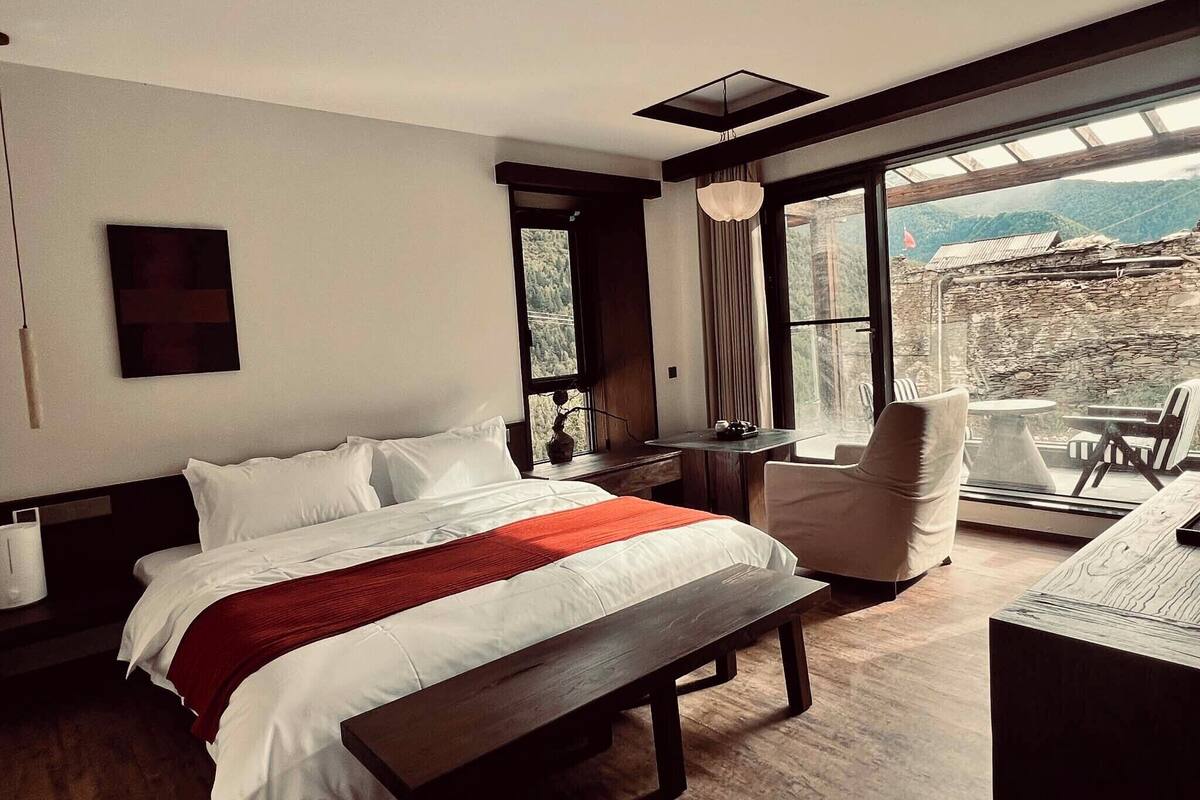 Quarto de hotel com uma cama grande, uma escrivaninha, uma cadeira e vista para as montanhas.