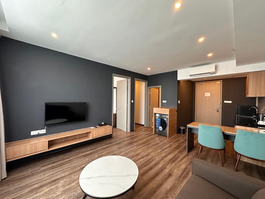 Um apartamento moderno com televisão de tela plana, uma sala de jantar com duas cadeiras, uma cozinha com geladeira preta, e máquina de lavar e secar embutidas.
