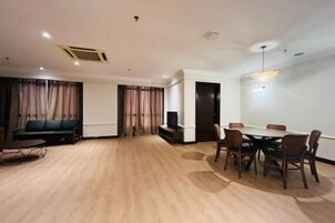 Uma sala de estar moderna com área de jantar, piso de madeira, um sofá, uma TV e um candelabro.