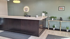 Uma área de recepção de hotel com um balcão escuro, um letreiro de neon e uma pequena planta no balcão.