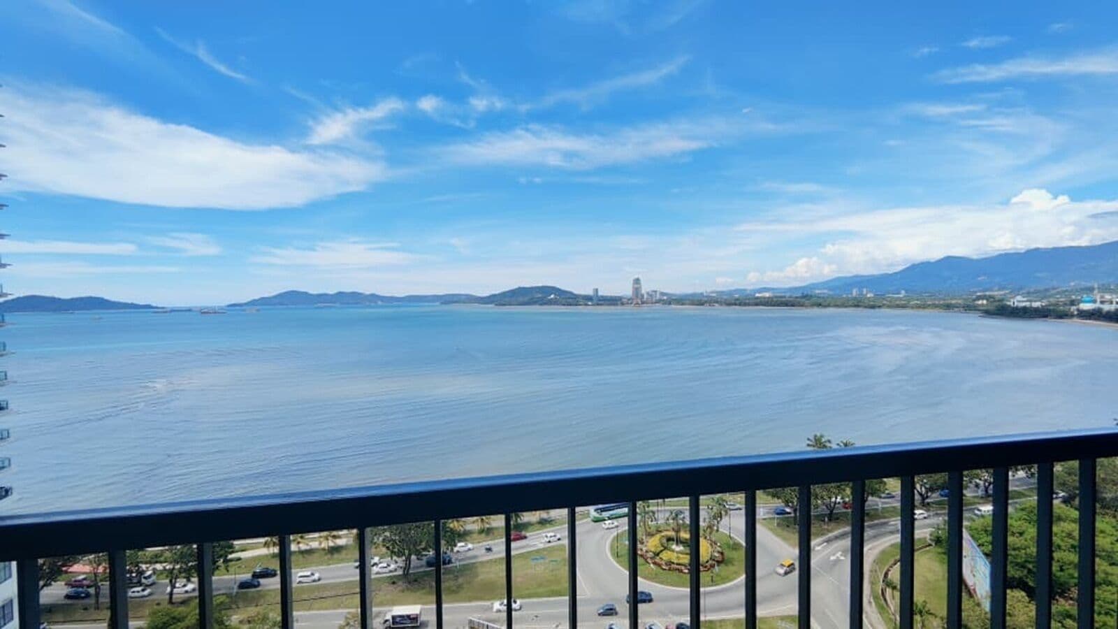 Vista de uma varanda com vista para águas calmas, uma paisagem urbana ao longe e um céu claro.