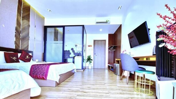 Quarto de hotel moderno com uma cama grande, escrivaninha, cadeira, televisão e uma janela ampla.