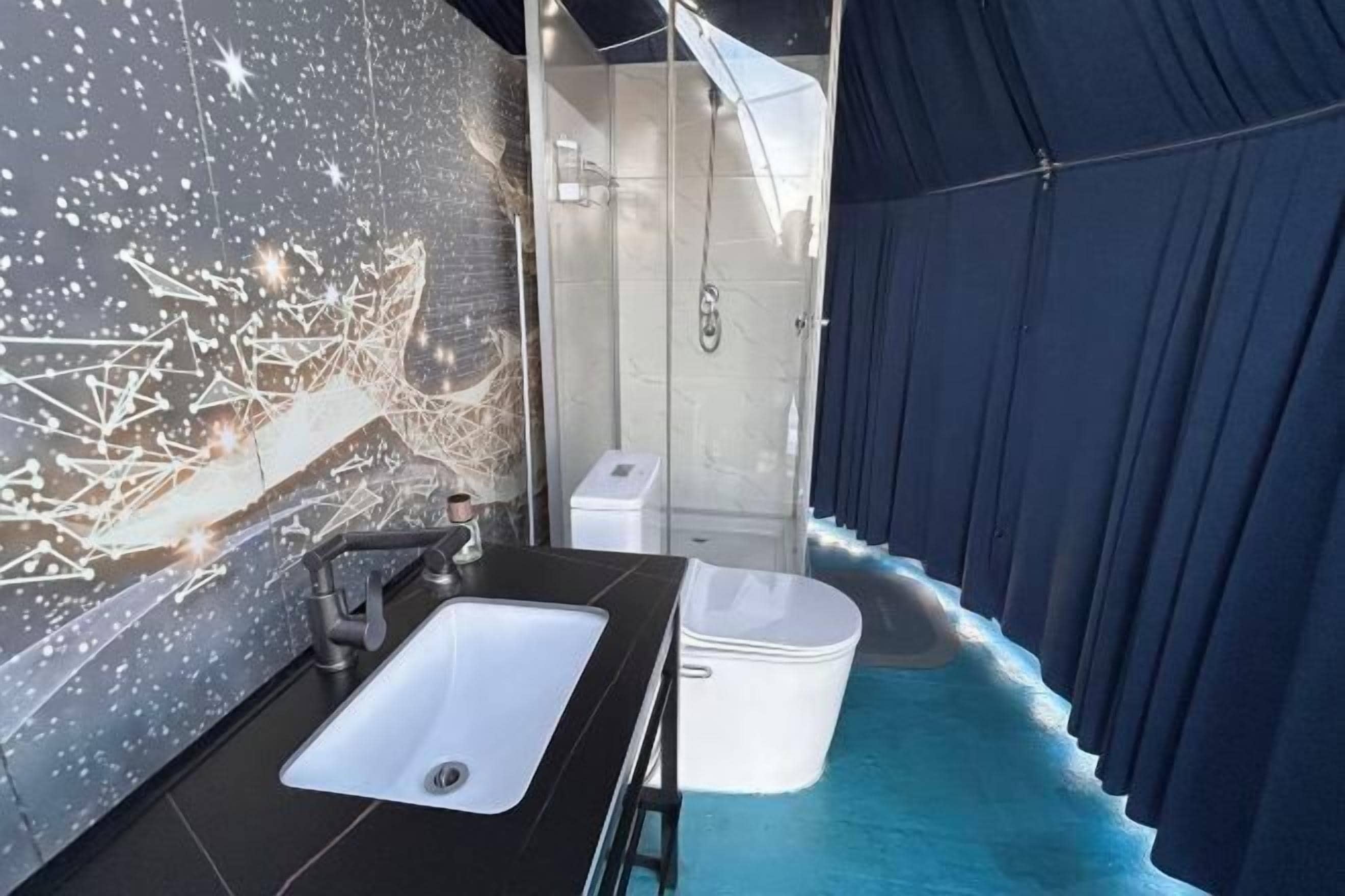 Uma casa de banho moderna com chuveiro em cabine de vidro, lavatório branco e chão em azulejos azuis.