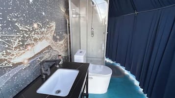 Uma casa de banho moderna com chuveiro em cabine de vidro, lavatório branco e chão em azulejos azuis.