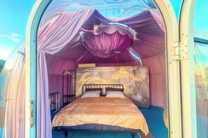 Um quarto tipo tenda com uma cama, cabeceira com mural de montanhas e cortinas roxas.