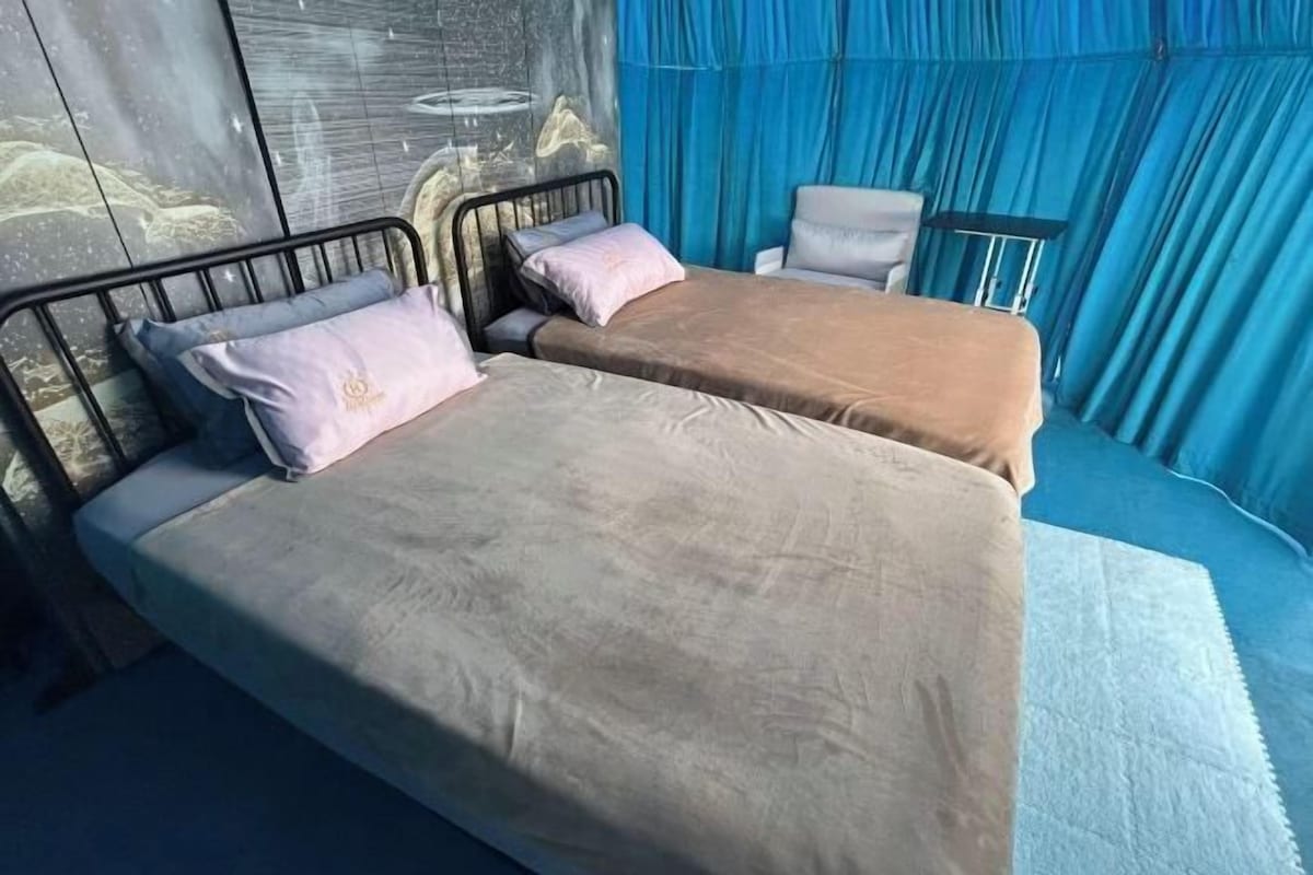 Quarto com duas camas, uma cadeira e uma mesinha.