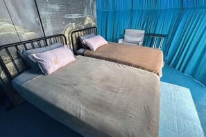 Quarto com duas camas, uma cadeira e uma mesinha.