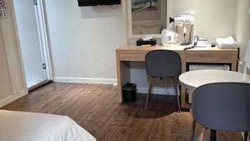 Quarto de hotel com cama, escrivaninha, cadeira, televisão, cafeteira e lixeira.