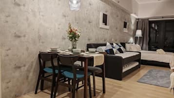 Uma sala de estar moderna com área de jantar, apresentando um sofá, uma mesa de jantar com cadeiras e um vaso com flores.
