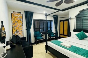 Quarto com cama de dossel, escrivaninha com cadeira, mesa com duas cadeiras e uma janela grande com cortinas.