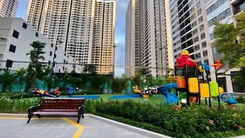 Área residencial com edifícios altos, um parquinho com equipamentos coloridos e um banco.