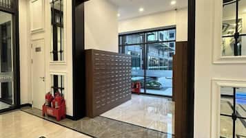 Um hall de hotel com balcão de recepção, extintor de incêndio e porta de vidro que dá para o exterior.