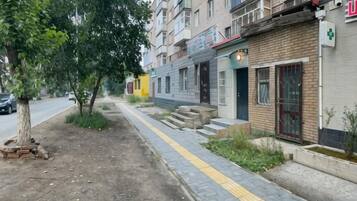 Uma rua residencial com prédios altos, calçada e uma árvore.