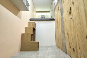 Um corredor estreito com degraus de madeira que levam a uma porta, parede de madeira e uma pequena estante com um aparelho de iluminação acima.